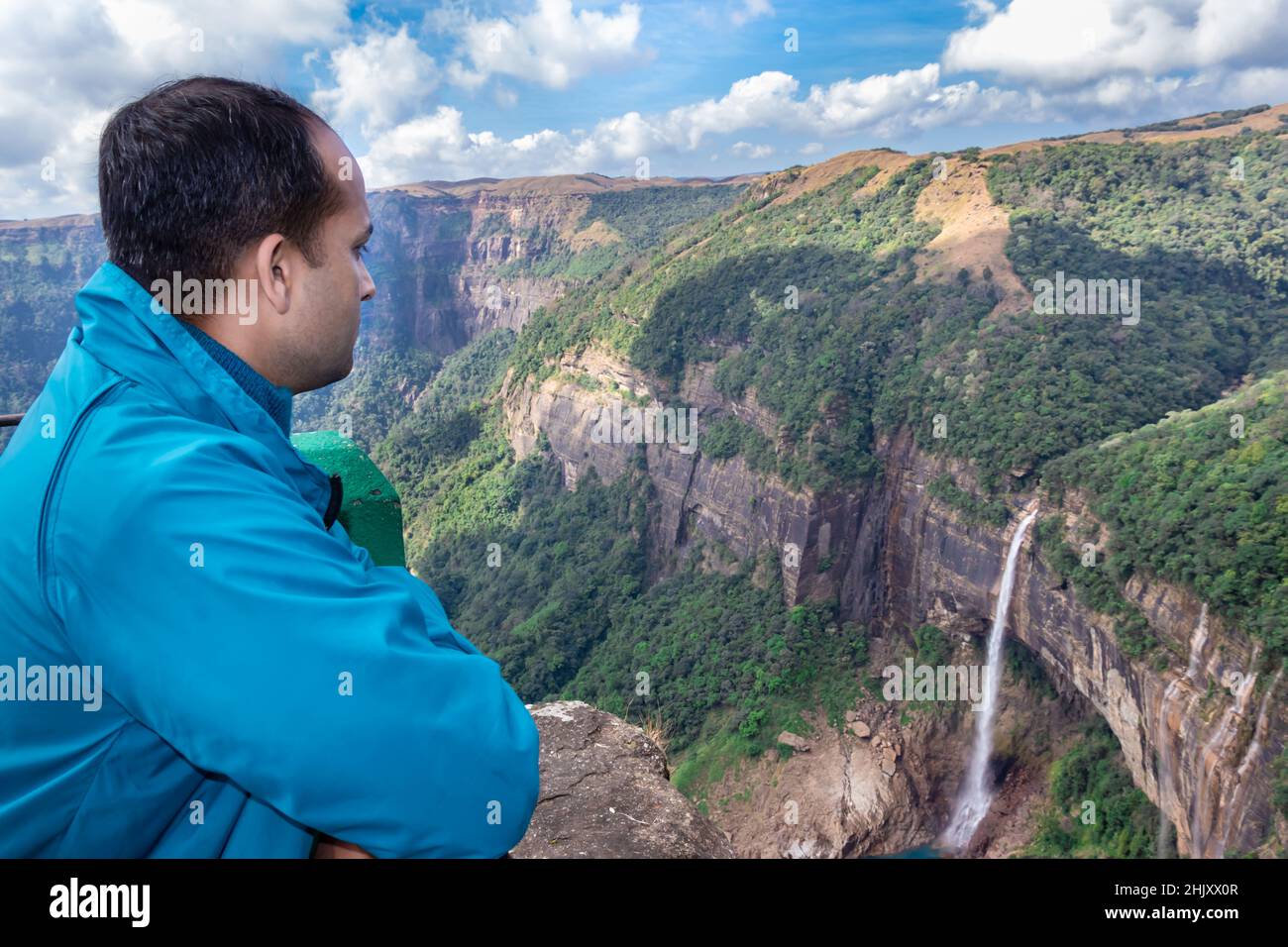 young man watching waterfall streams falling from mountain top covered ...