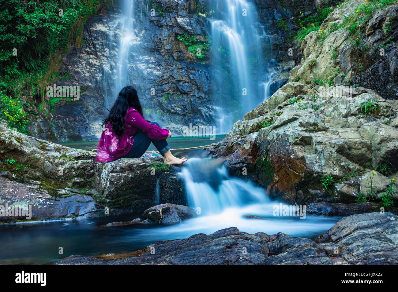 girl sitting on rock with waterfall falling from mountain with blurred ...