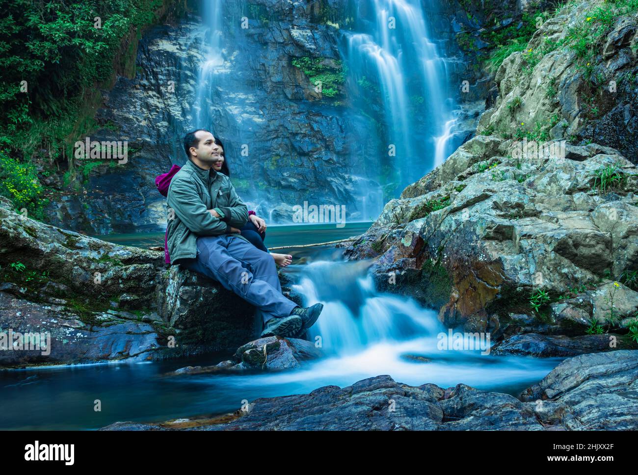 couple sitting on rock with waterfall falling from mountain with ...