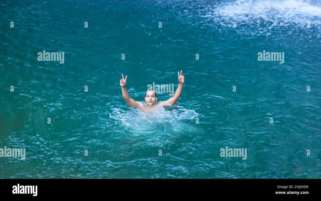 young man swimming at natural waterfall blue water at morning from top ...