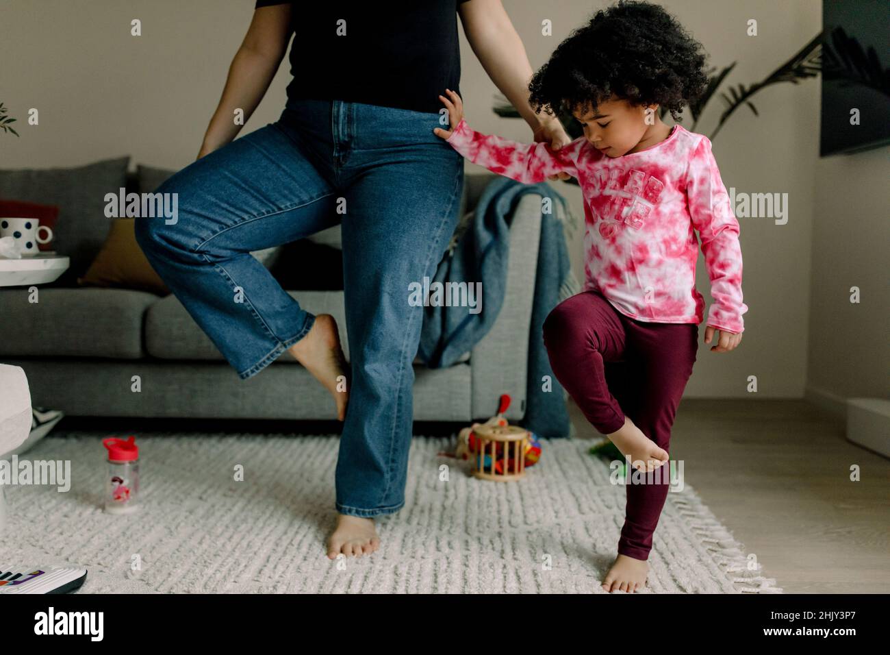 Low section of mother teaching tree pose to daughter at home Stock ...