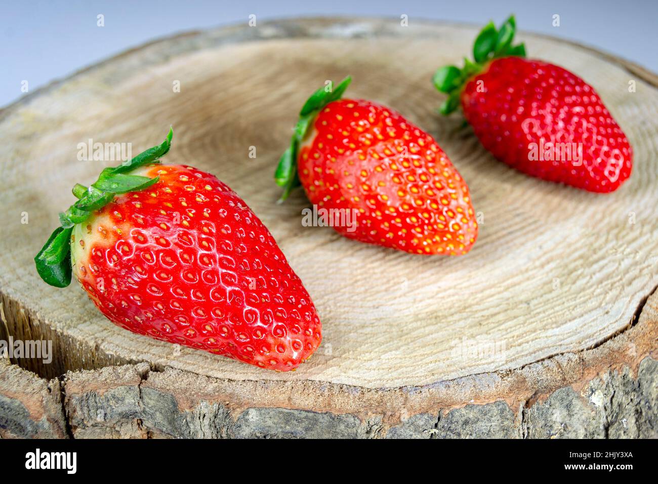 Strawberry. Set of three ripe strawberries on a brown wooden log ...