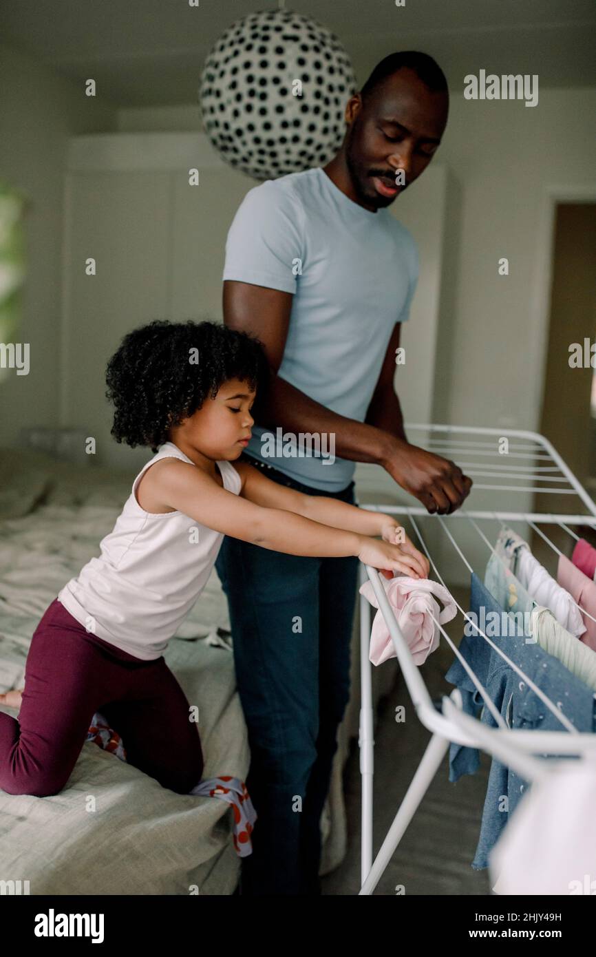 Daughter learning to arrange clothes on drying stand by father at home ...
