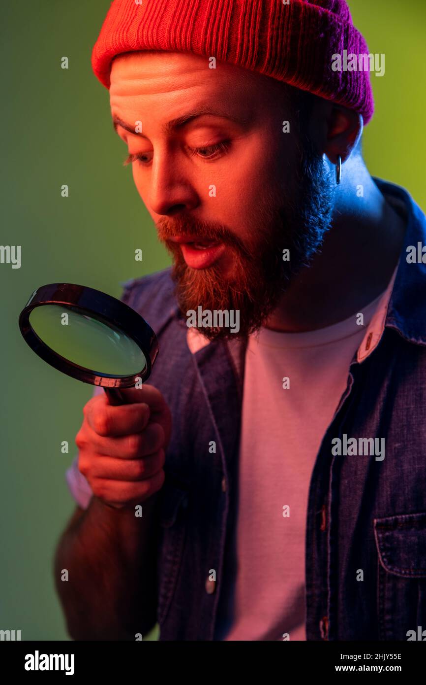 Hipster guy looking through magnifying glass, spying, finding out ...