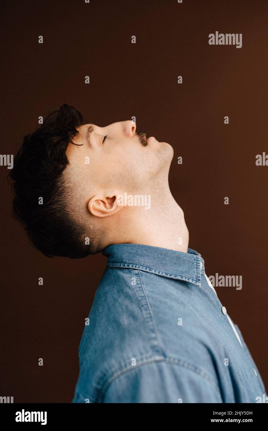 Side view of young man by brown background Stock Photo - Alamy