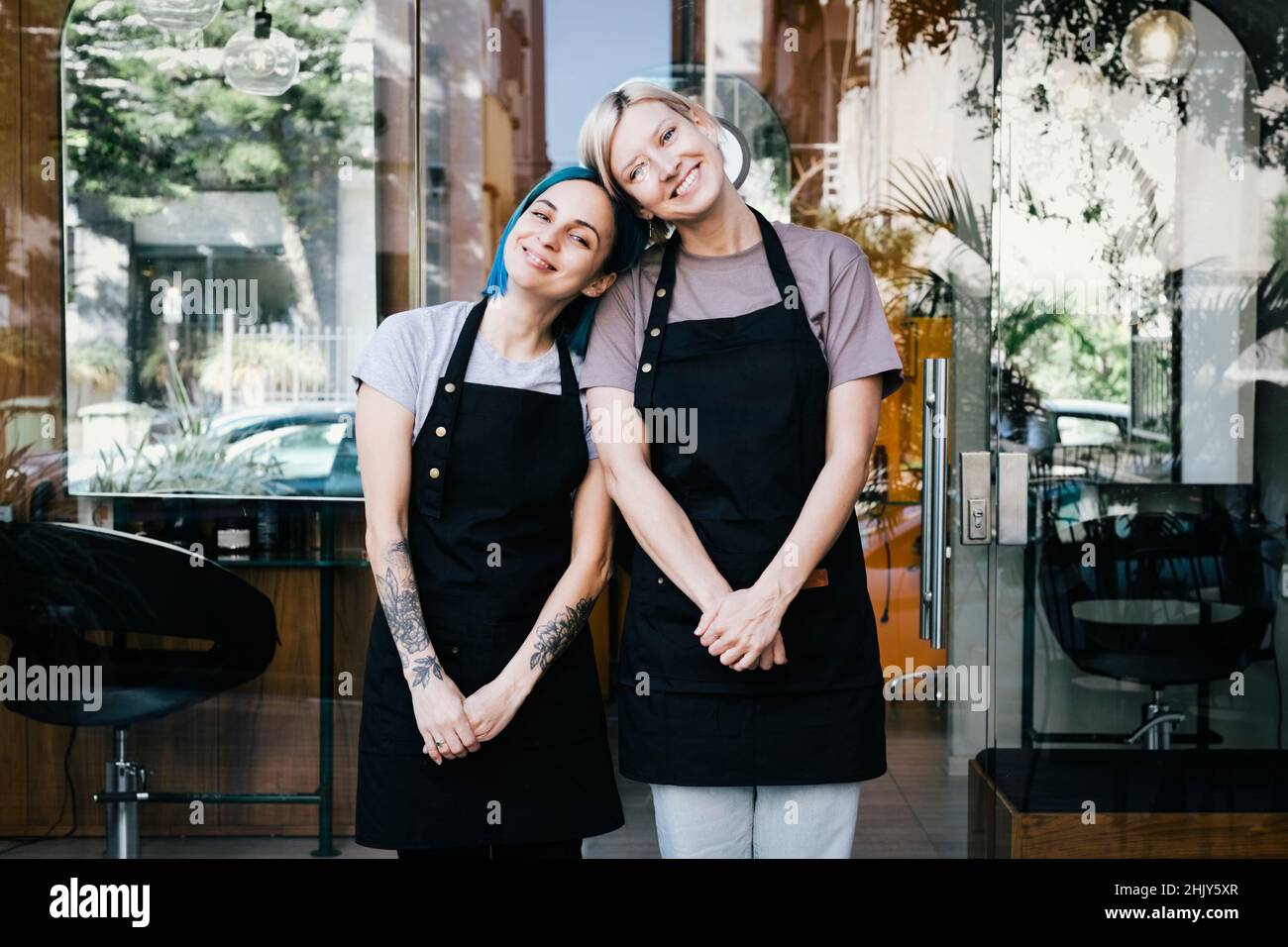Portrait of smiling female colleagues standing against hair salon Stock ...