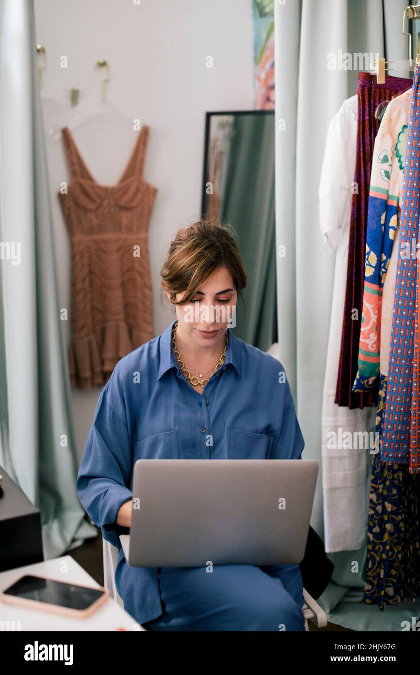 Female entrepreneur using laptop while working in clothing store Stock ...
