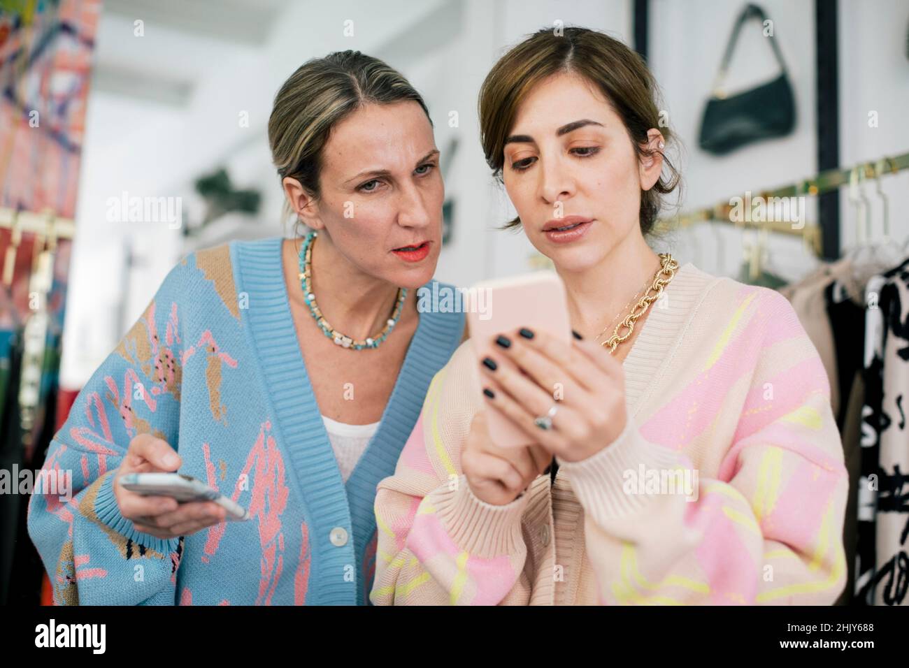 Female colleagues using smart phone in clothing store Stock Photo - Alamy