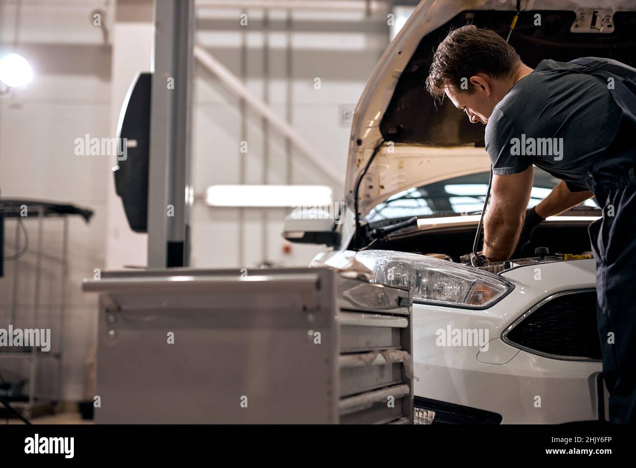 rear view on Mid adult mechanic repairing system of car in hood in auto ...