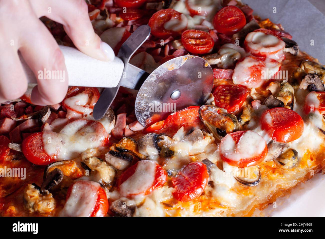 Hand with pizza cutter knife cutting pizza at kitchen table. Close up ...
