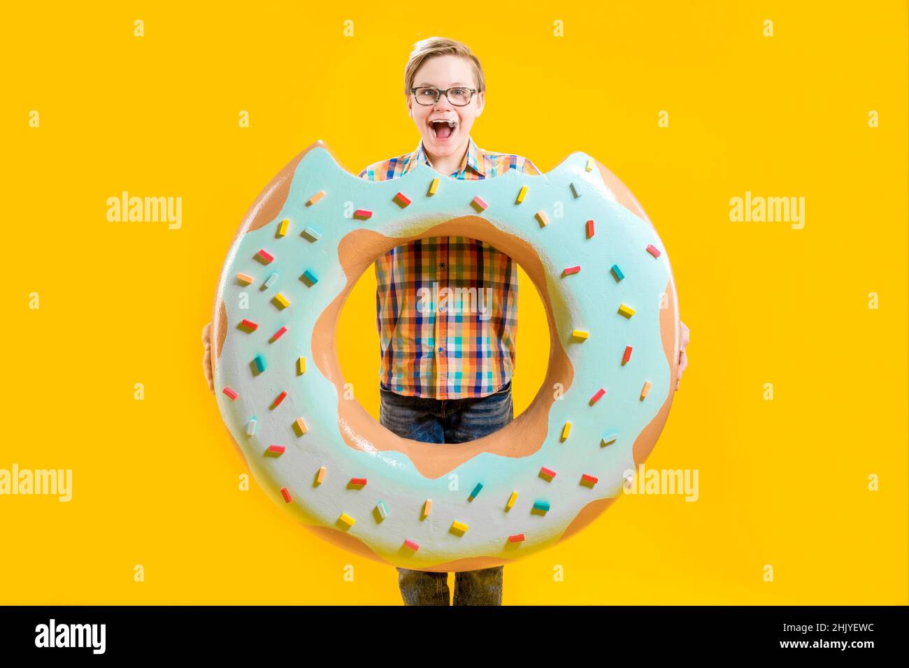 A cute boy is holding a huge donut in his hands, trying to bite him ...