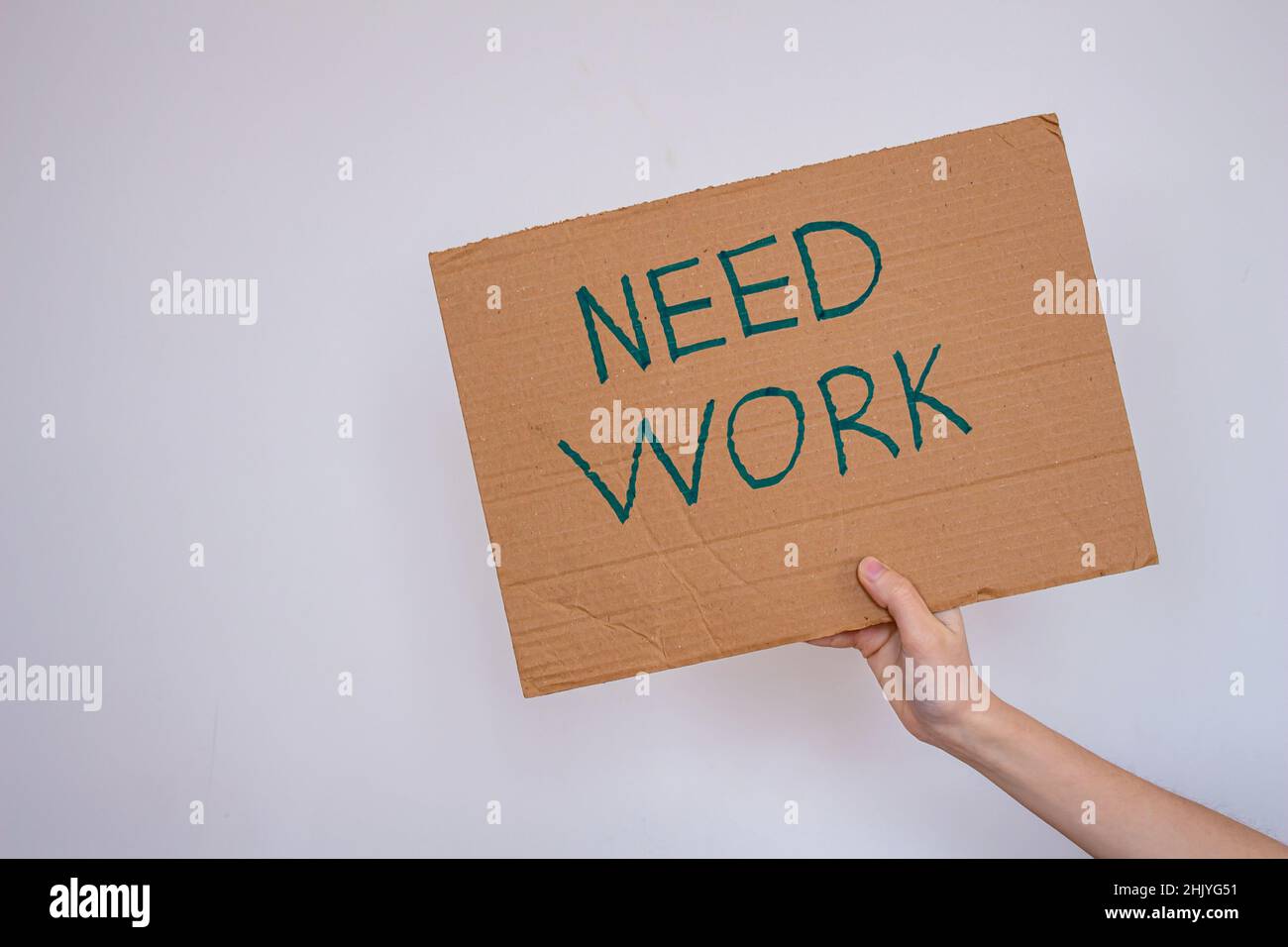 Hand holding cardboard with need work inscription over gray wall ...