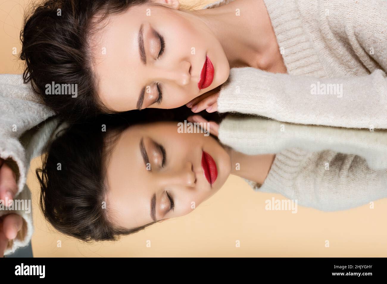 Stylish model in sweater closing eyes while lying on mirror isolated on ...