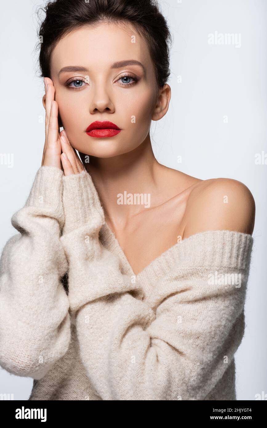 Trendy model in sweater touching face and looking at camera isolated on ...