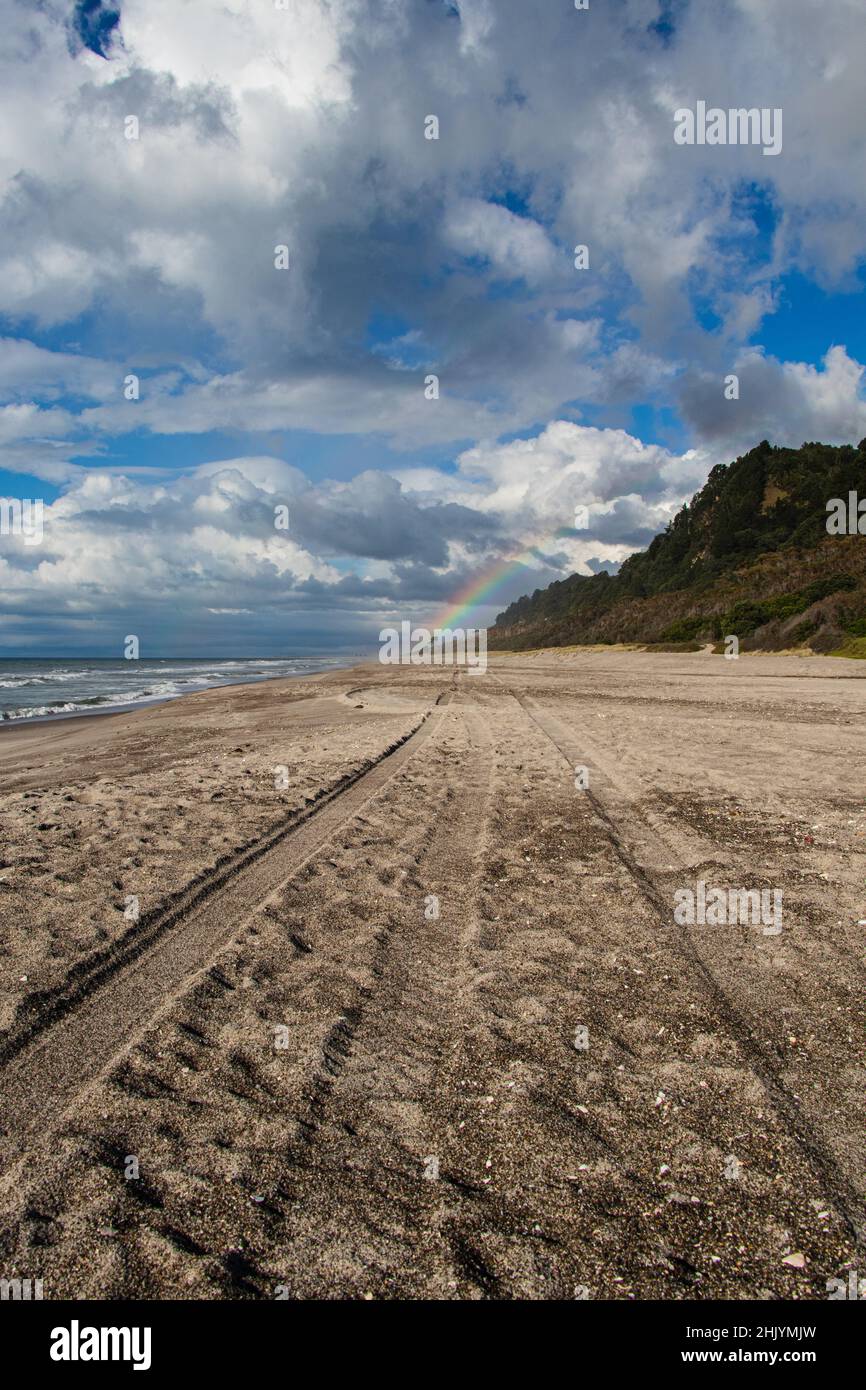 Vertical shot of a coastline with clouds and rainbow in the background ...