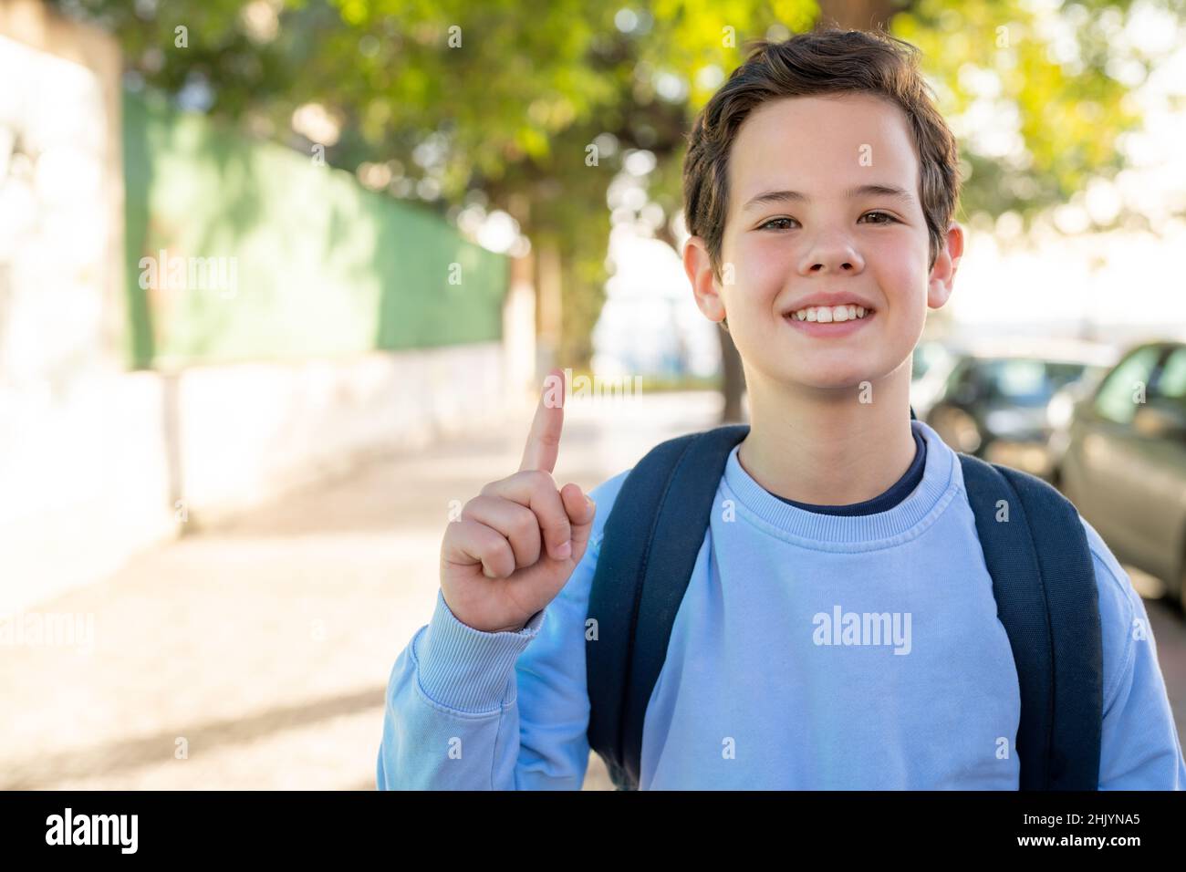 Close up portrait of cute smiling boy with backpack outside of school ...