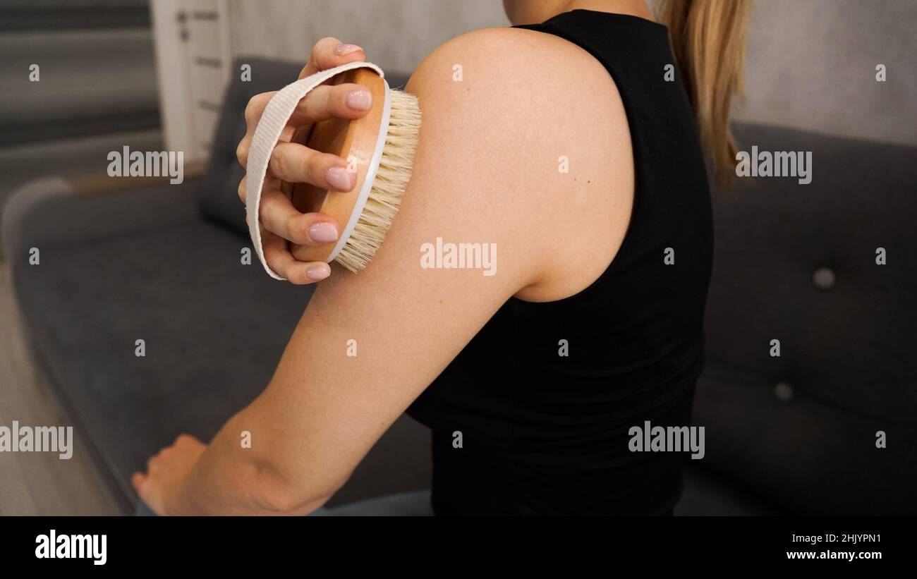 Young woman uses a dry brush to self-massage her arms and shoulders ...