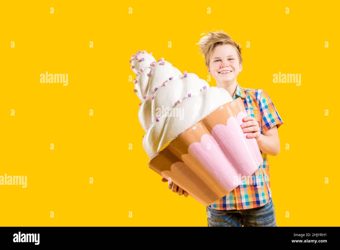 A cute boy is holding a huge cupcake in his hands. Cheerful teenager ...
