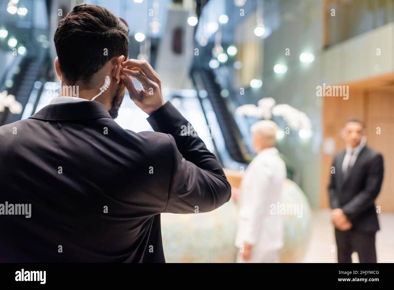 back view of bi-racial security man adjusting earpiece near blurred ...