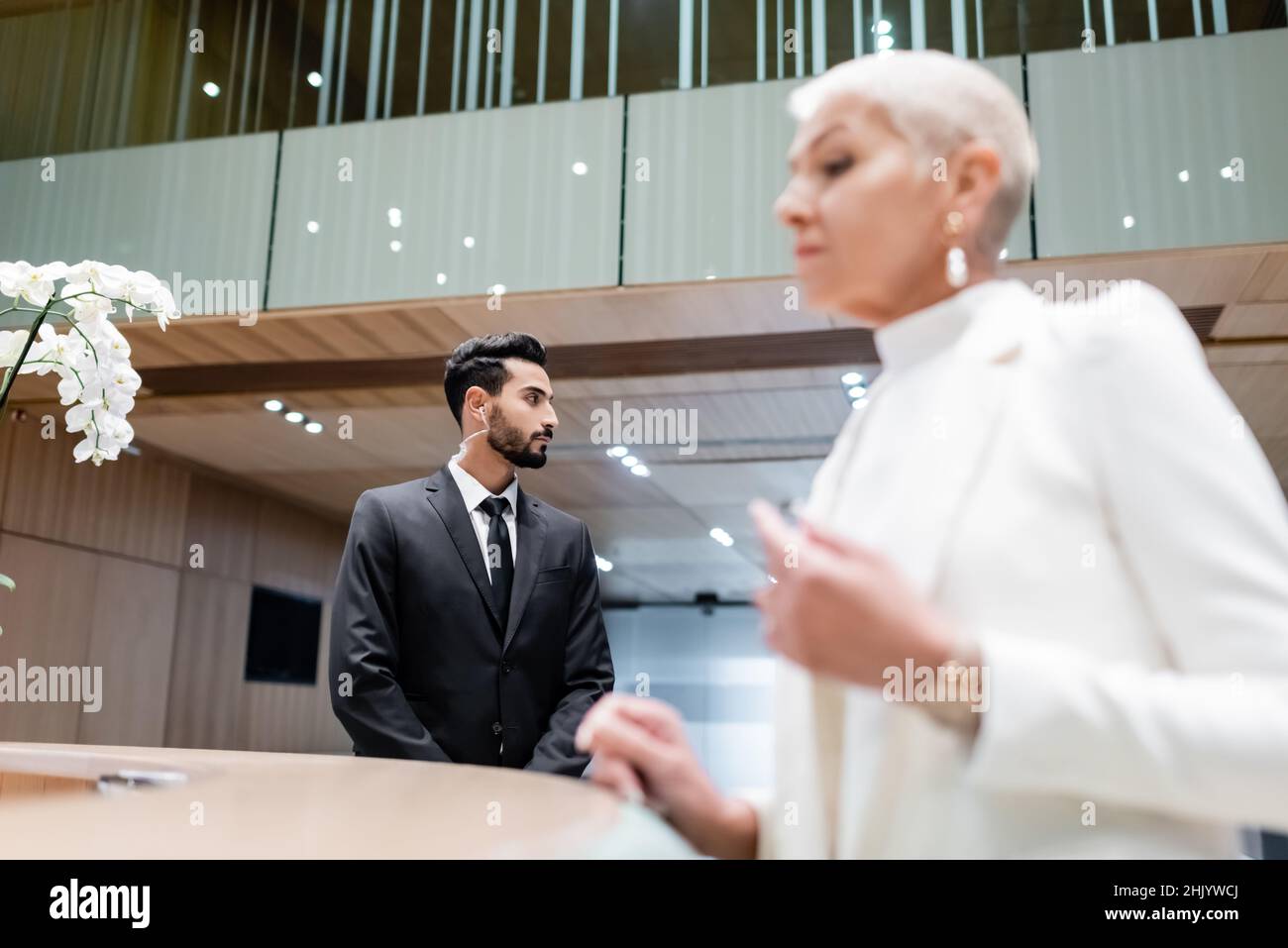 bi-racial bodyguard looking away while blurred business lady checking ...