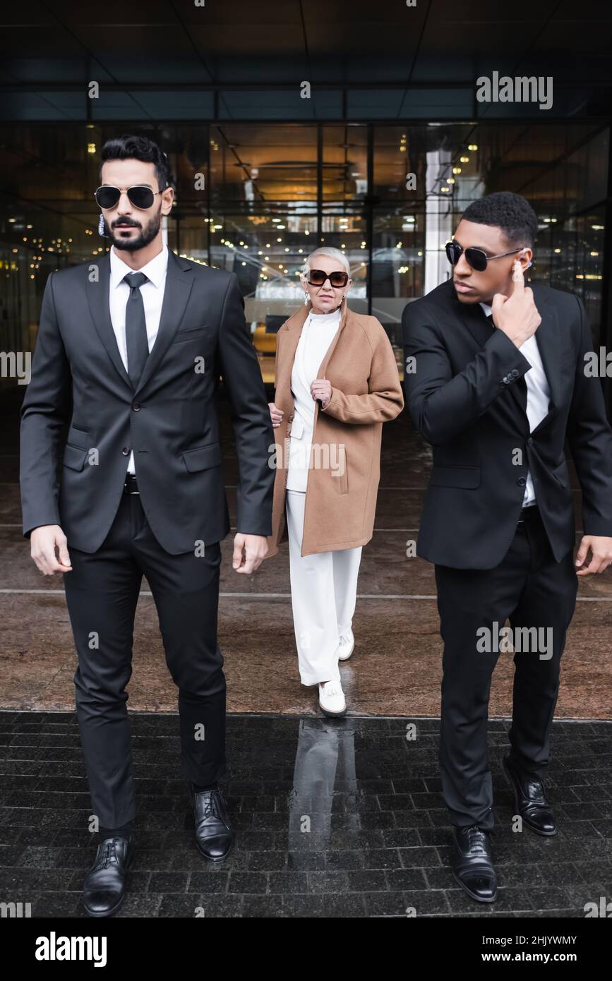 interracial bodyguards in sunglasses escorting stylish businesswoman ...