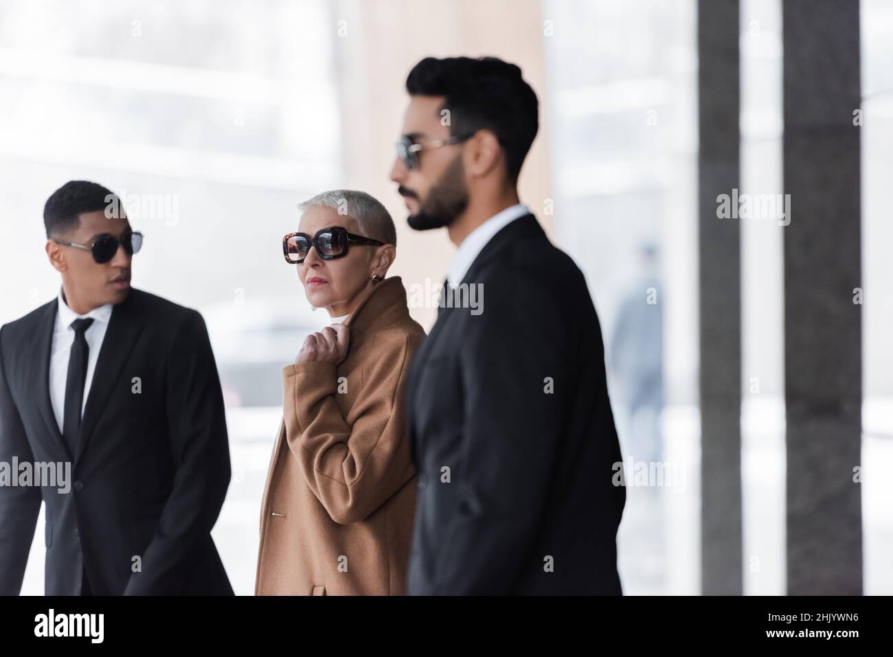 blurred multiethnic bodyguards escorting stylish senior businesswoman ...