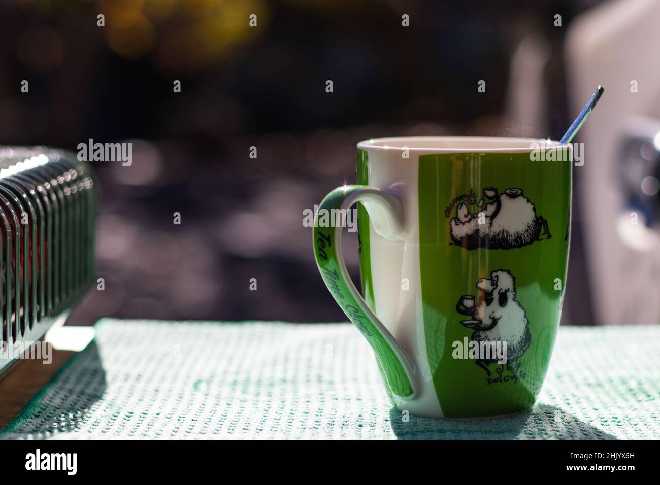 Shallow focus shot of a green mug with sheep illustrations and a spoon ...
