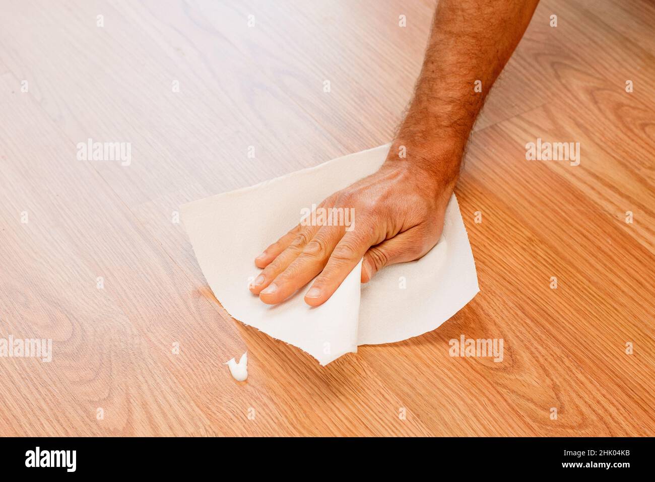 A man's hand wiping a white cream stain on the wooden floor with a ...