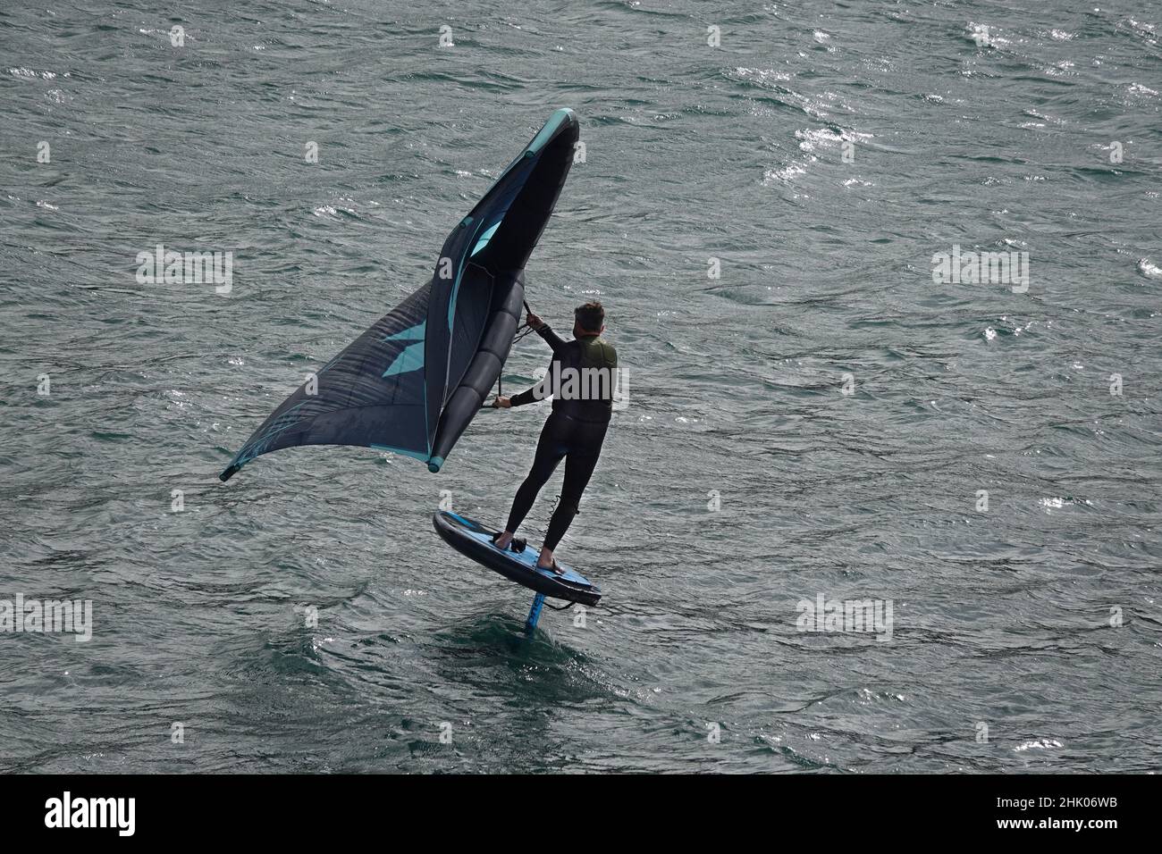 A male wing surfer surfing or wing foiling with an inflatable wing in ...