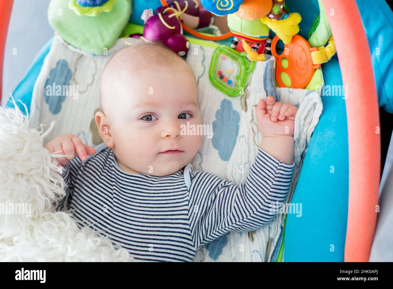 Portrait of a baby boy, lying down on a playmat with soft toys around ...