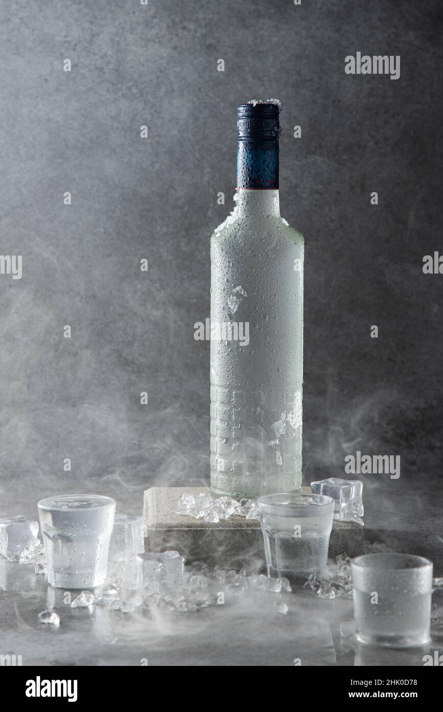 Ice-cold bottle of vodka with shot glasses on gray background with copy ...