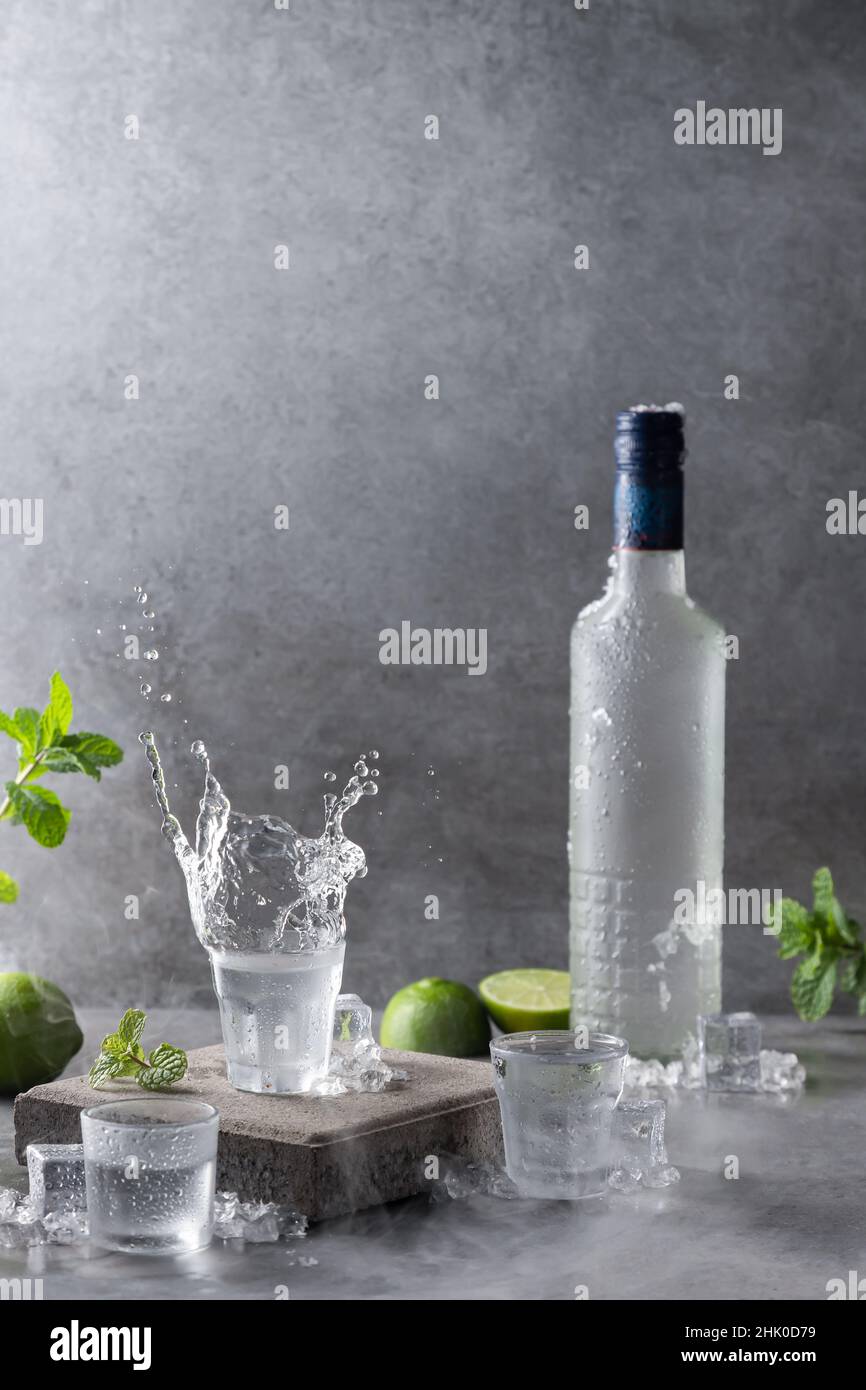 Bottle of vodka with splash shot glass on concrete background with ...