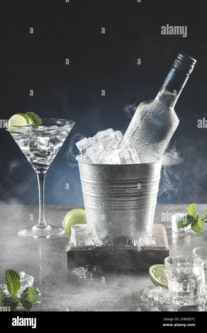 Bottle of ice cold vodka in bucket of ice and glasses on dark ...