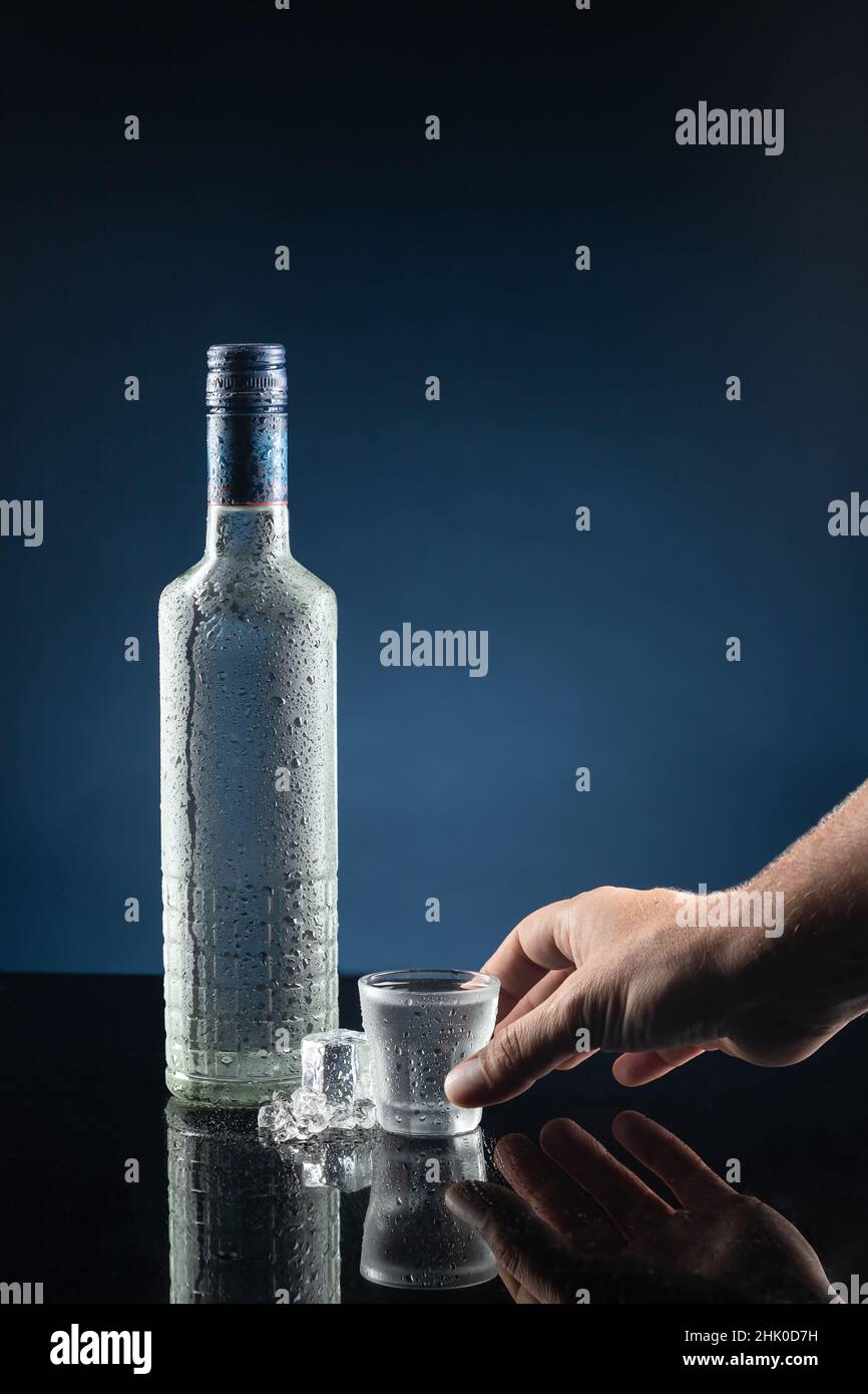Hand taking a shot of vodka on dark blue background. Vertical format ...