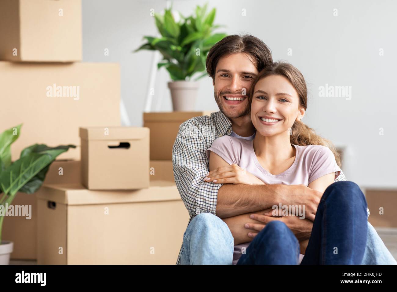 Cheerful millennial caucasian guy hugging woman sit among boxes, plants ...