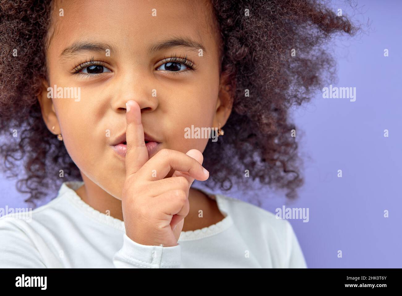 Adorable black little girl holding finger on lips symbol of hush ...