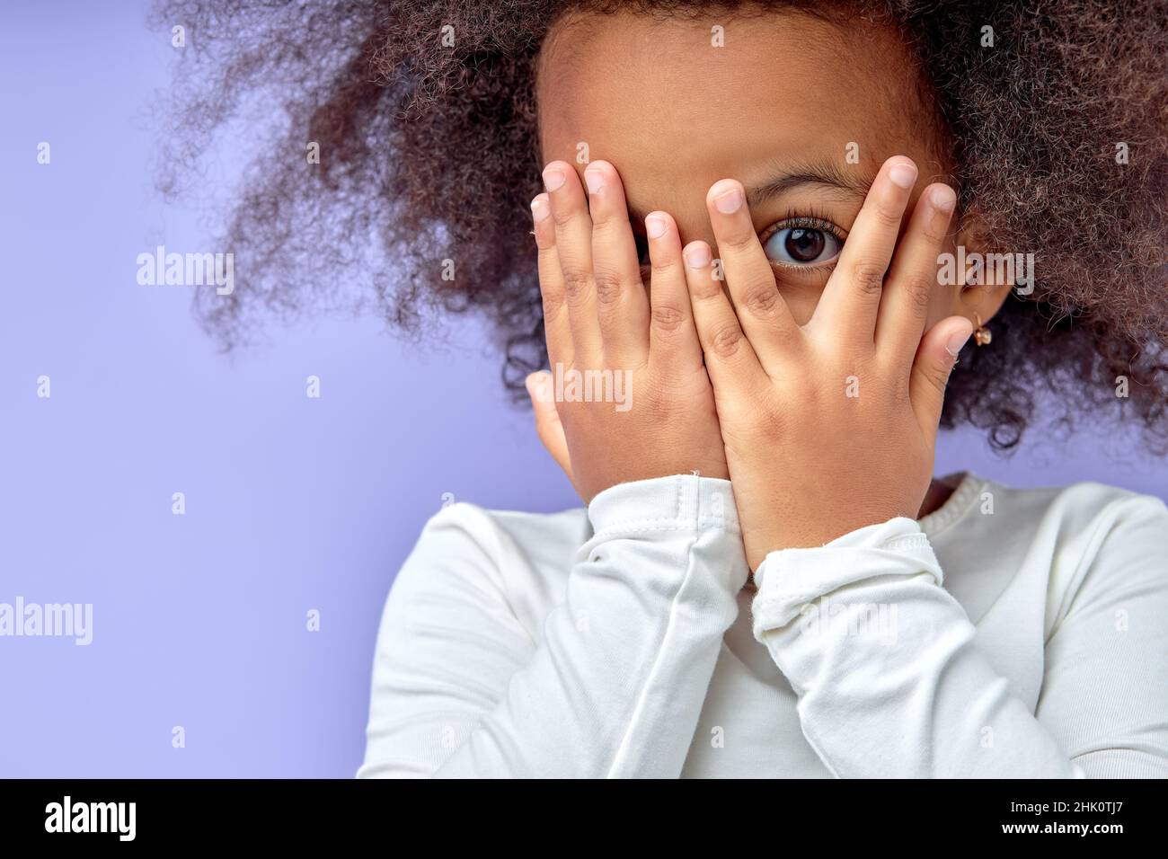 emotional little black girl covers face with hand isolated over purple ...