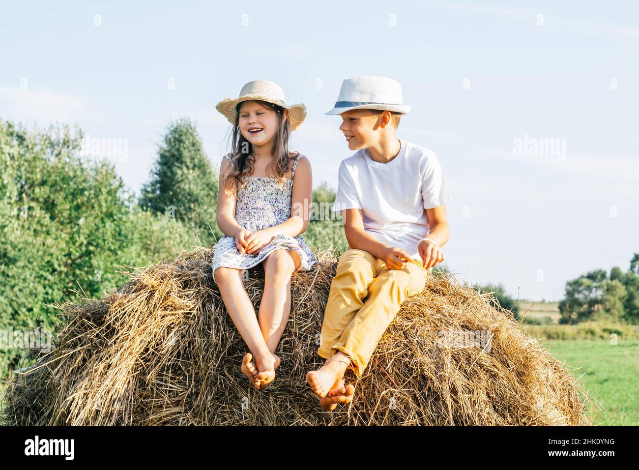 Portrait of two barefoot children boy and girl sitting on haystack in ...
