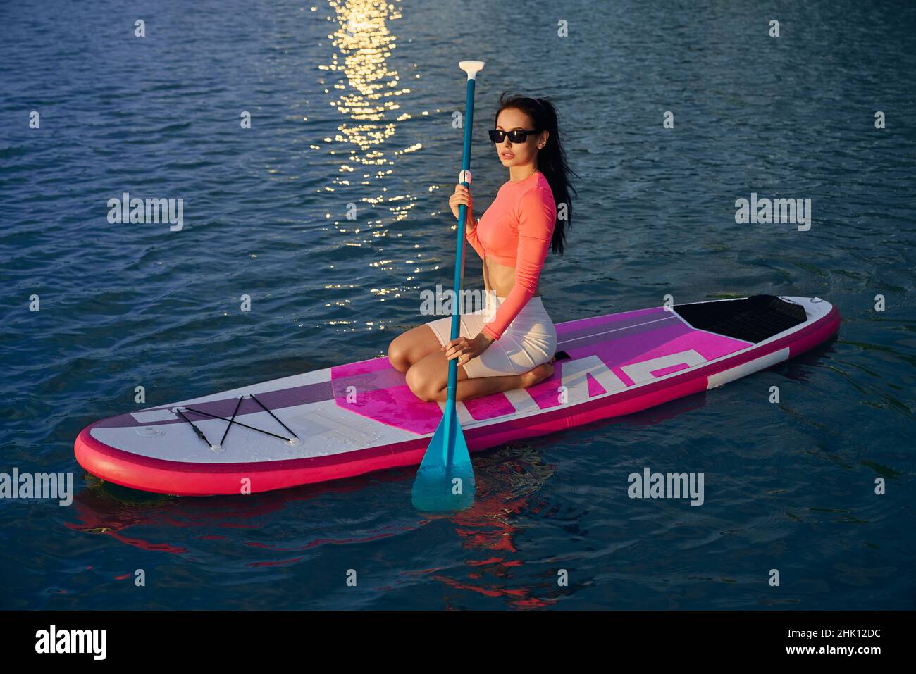 Beautiful female athlete in sunglasses and sport outfit swimming on sup ...