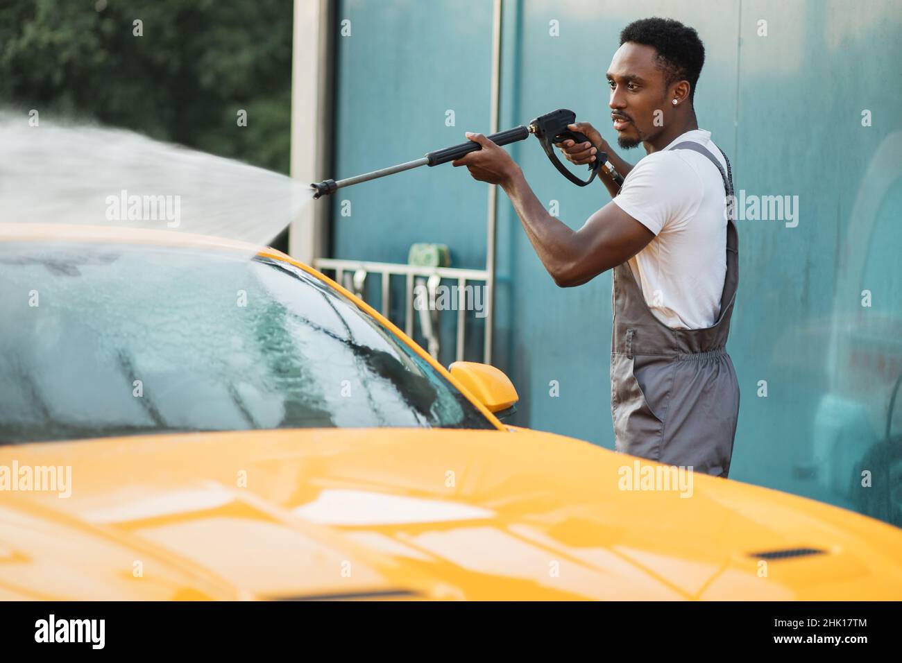 Manual car wash. Handsome African young man washing his luxury yellow ...