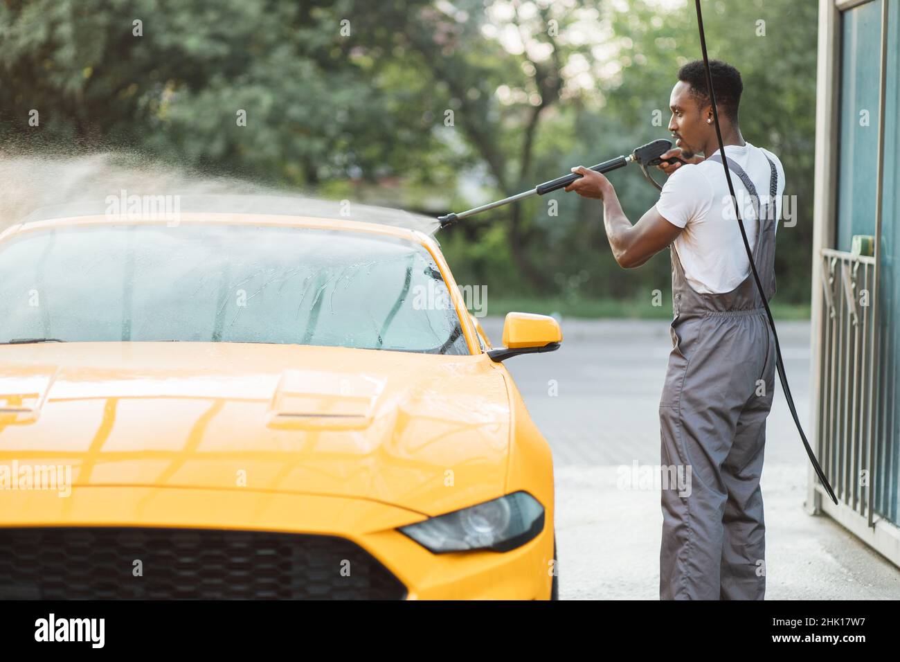 Manual car wash. Handsome African young man washing his luxury yellow ...