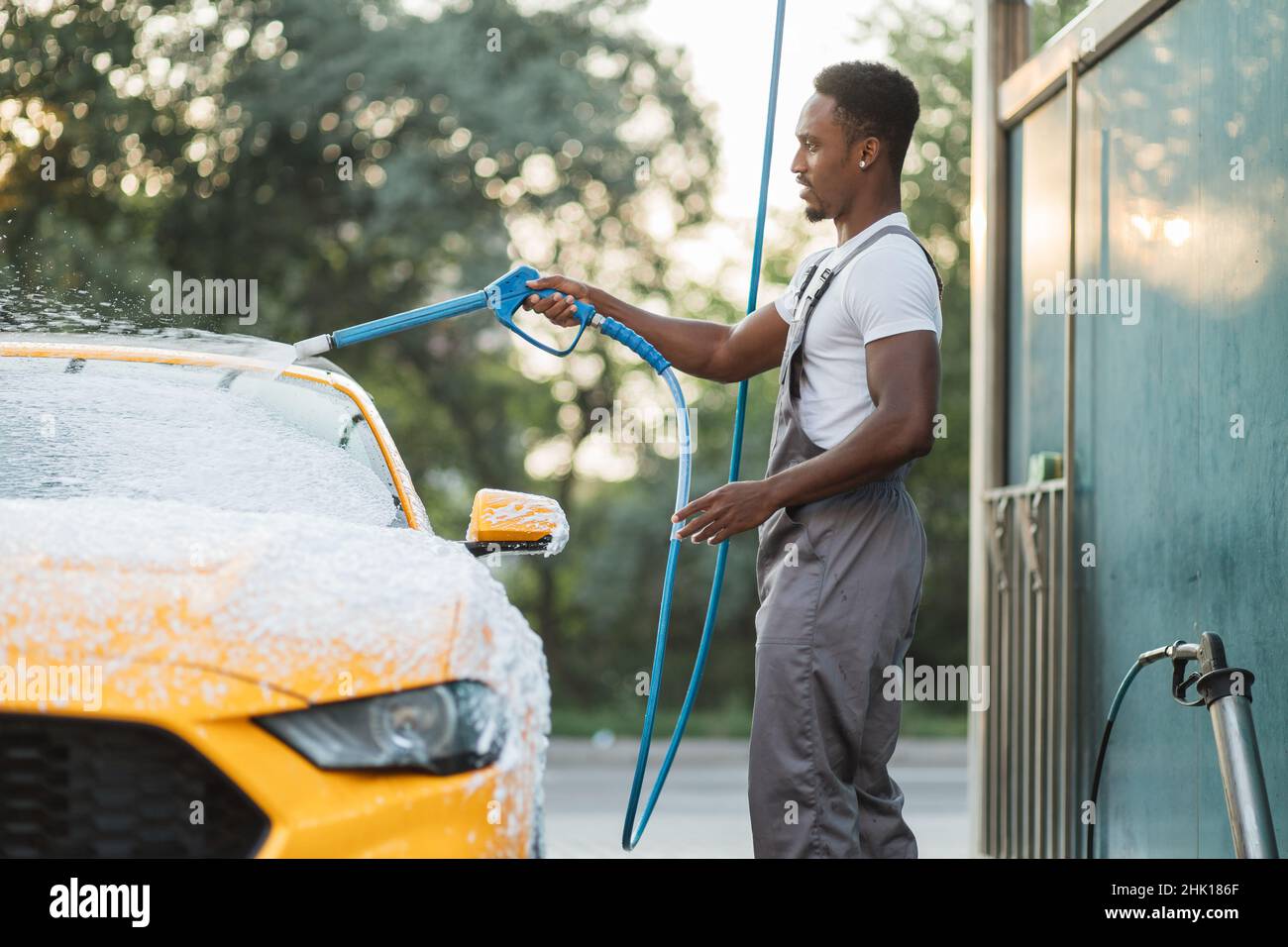 Portrait of handsome bearded young African man washing his yellow car ...
