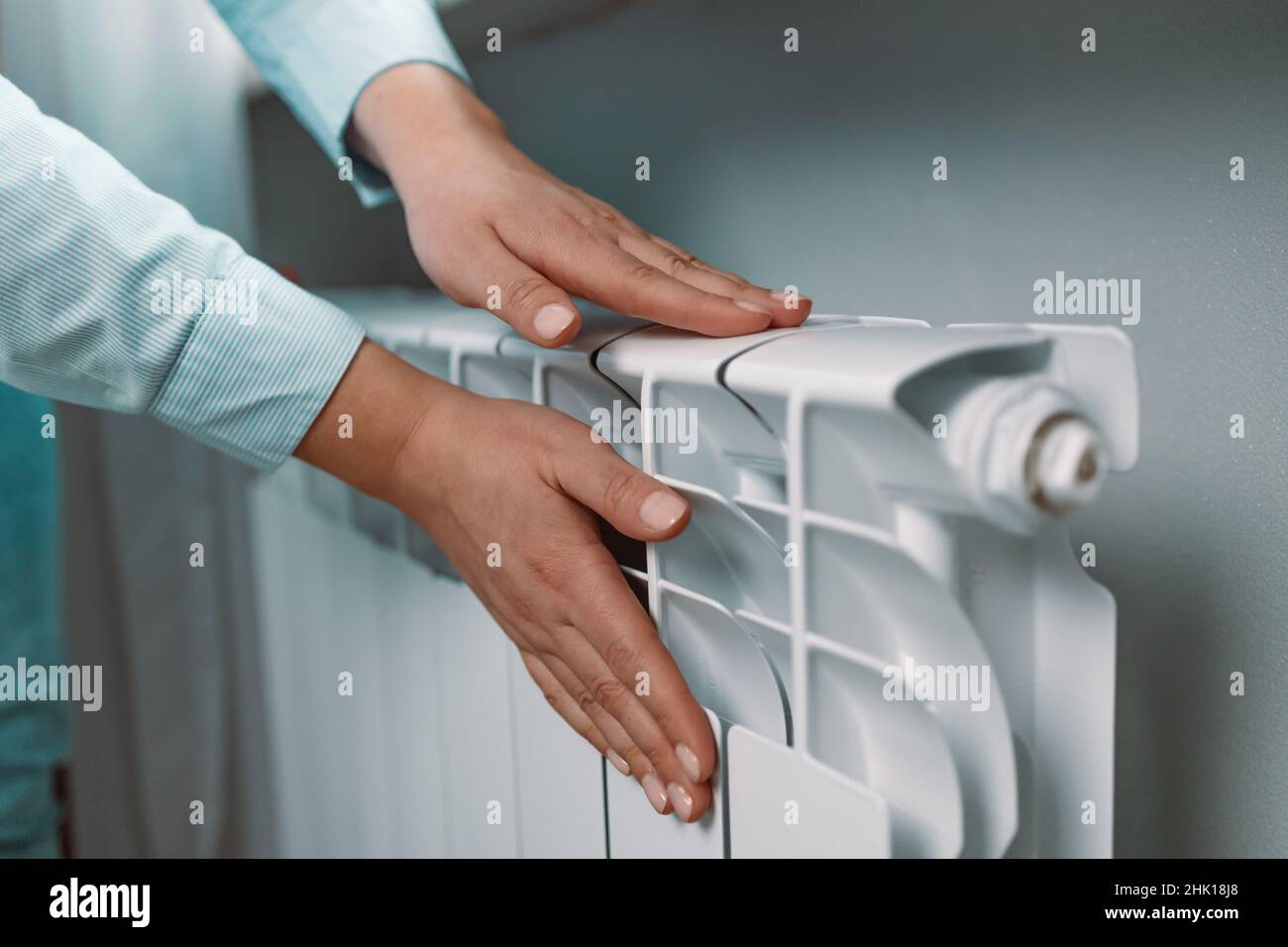 Female hands are touching the white heating radiator in the house ...