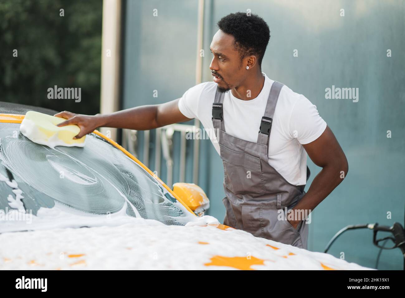 Young attractive African American man washing his yellow luxury car in ...