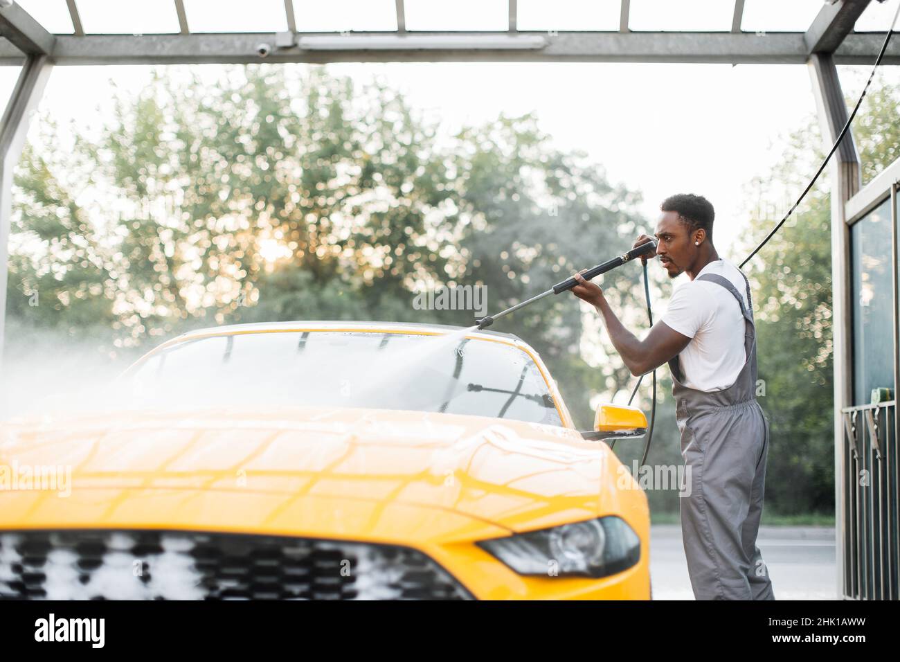 Manual car wash. Handsome African young man washing his luxury yellow ...