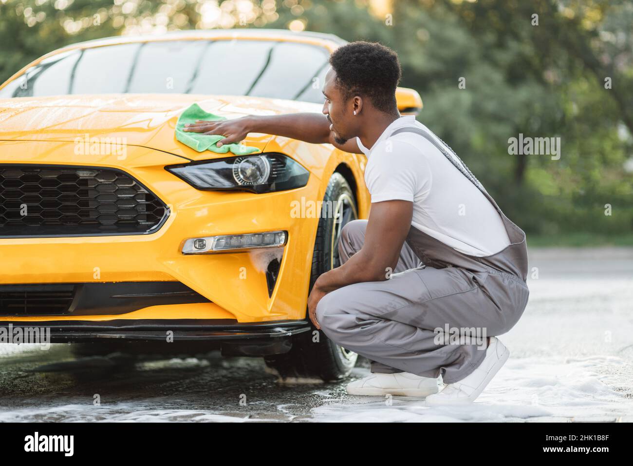 Young African man washing and wiping modern sport yellow car hood at ...