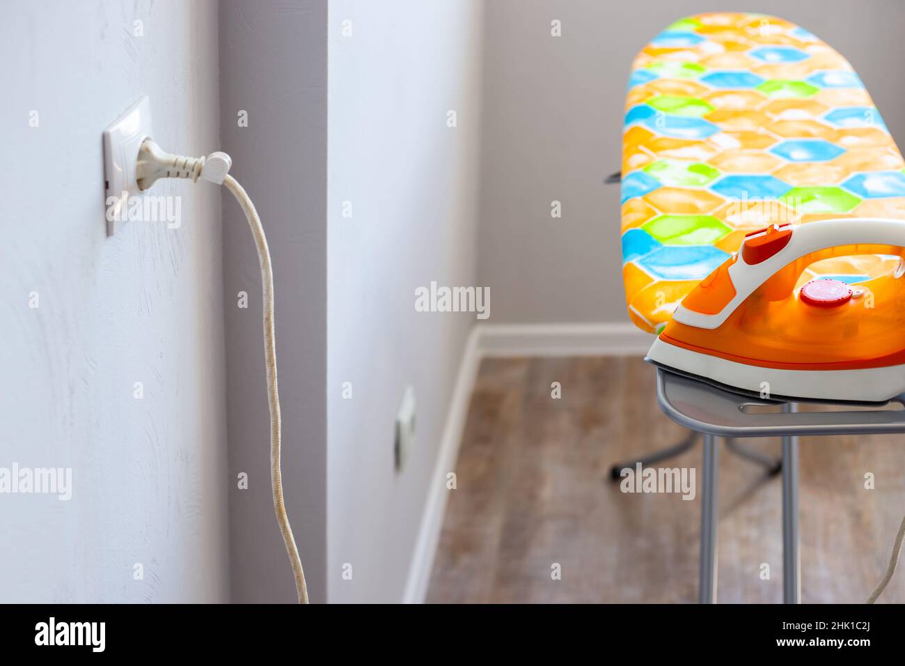 Electric iron plugged into the socket on the ironing board in the ...