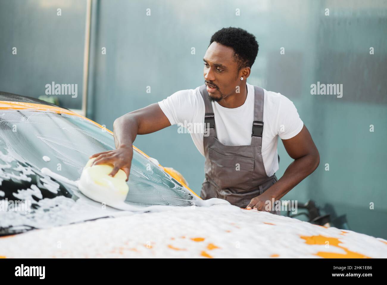 Young attractive African American man washing his yellow luxury car in ...
