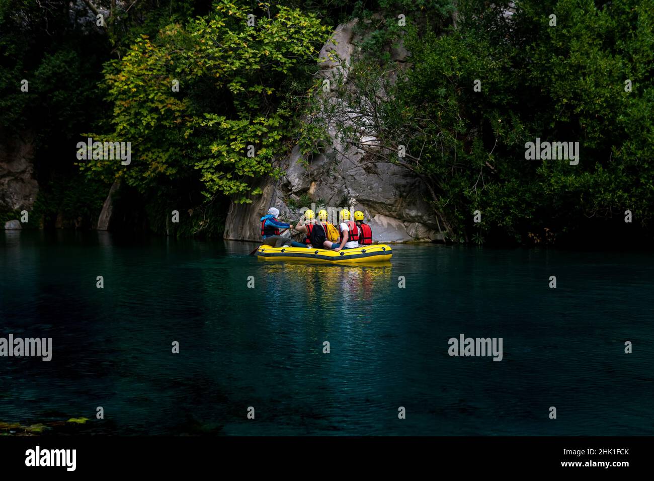 tourists on an inflatable boat float down a rocky canyon with blue ...