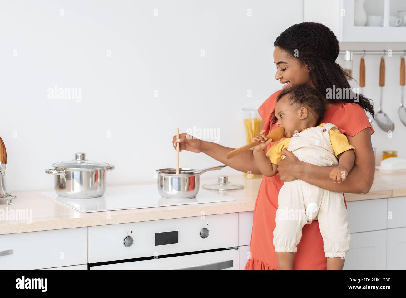 Beautiful Black Mom Cooking Food In Kitchen With Little Son In Arms ...
